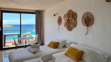 Quarto de hotel com duas camas, vista para o mar e varanda com mobiliário de exterior.