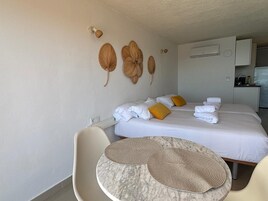 Quarto de hotel com cama, duas almofadas, mesa redonda com jogo americano, uma cadeira e arte decorativa na parede.