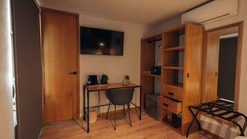 Quarto compacto com escrivaninha de madeira, cadeira, mesa pequena com chaleira, micro-ondas e guarda-roupa embutido.