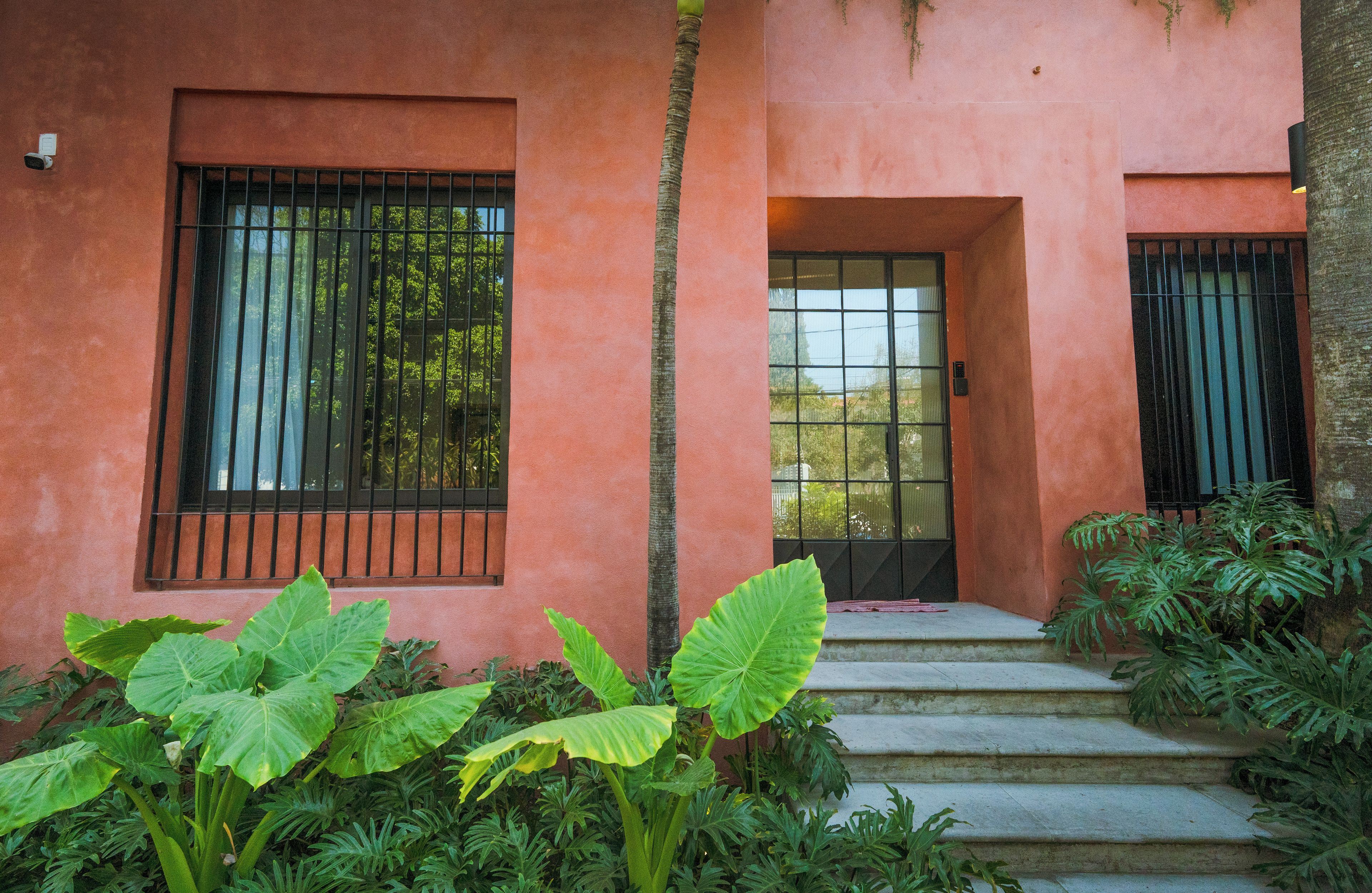 Um edifício com fachada rosa, grandes janelas com barras pretas e uma escadaria que leva à entrada.