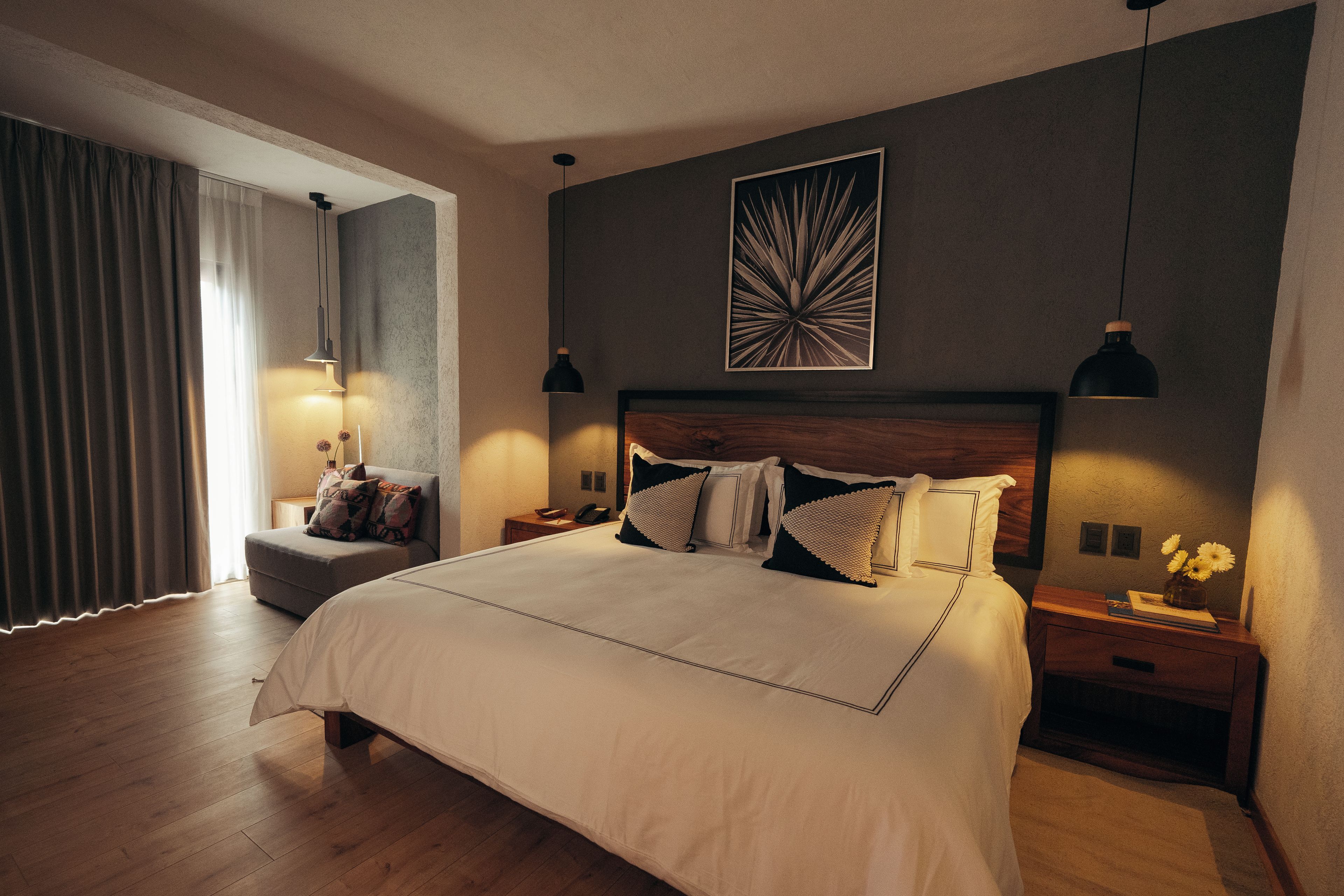 Quarto de hotel com cama grande, mesas de cabeceira, um criado-mudo, obra de arte na parede e janela com cortinas.