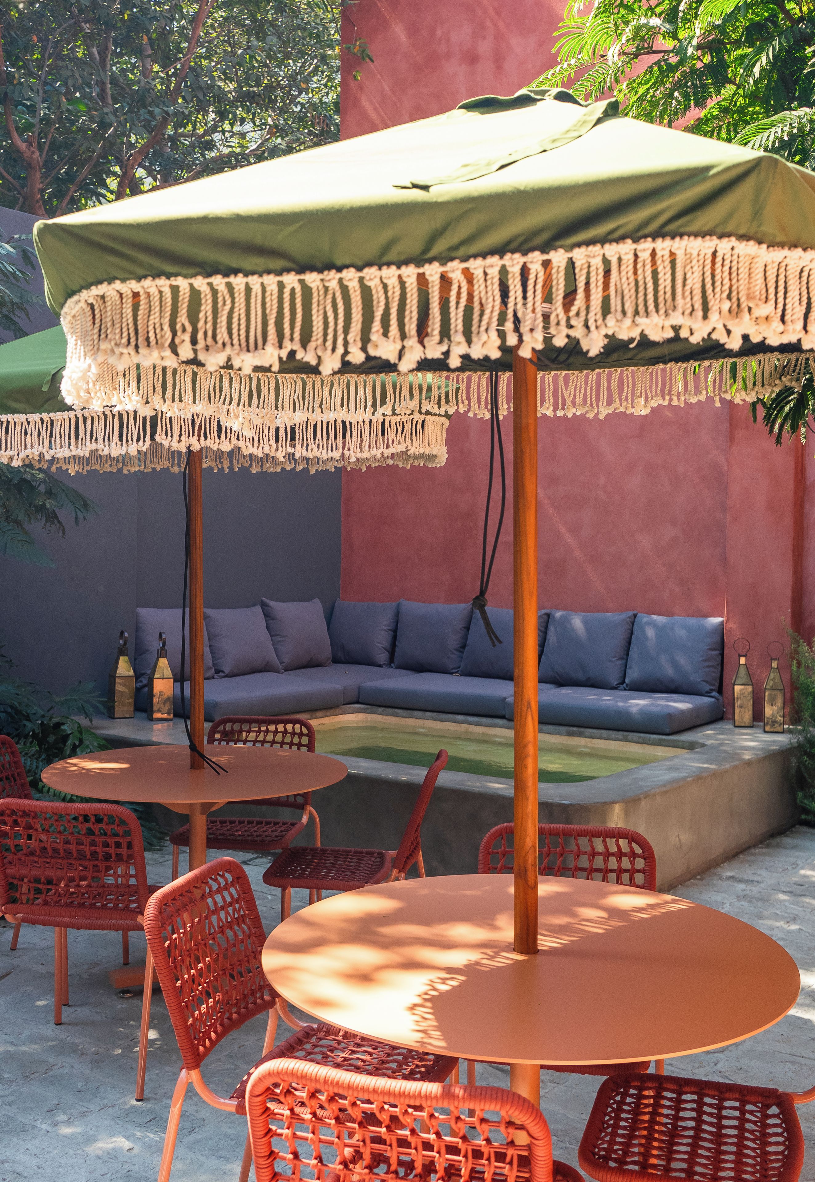 Uma área de estar ao ar livre com mesas e cadeiras redondas, um sofá e um guarda-sol decorativo.