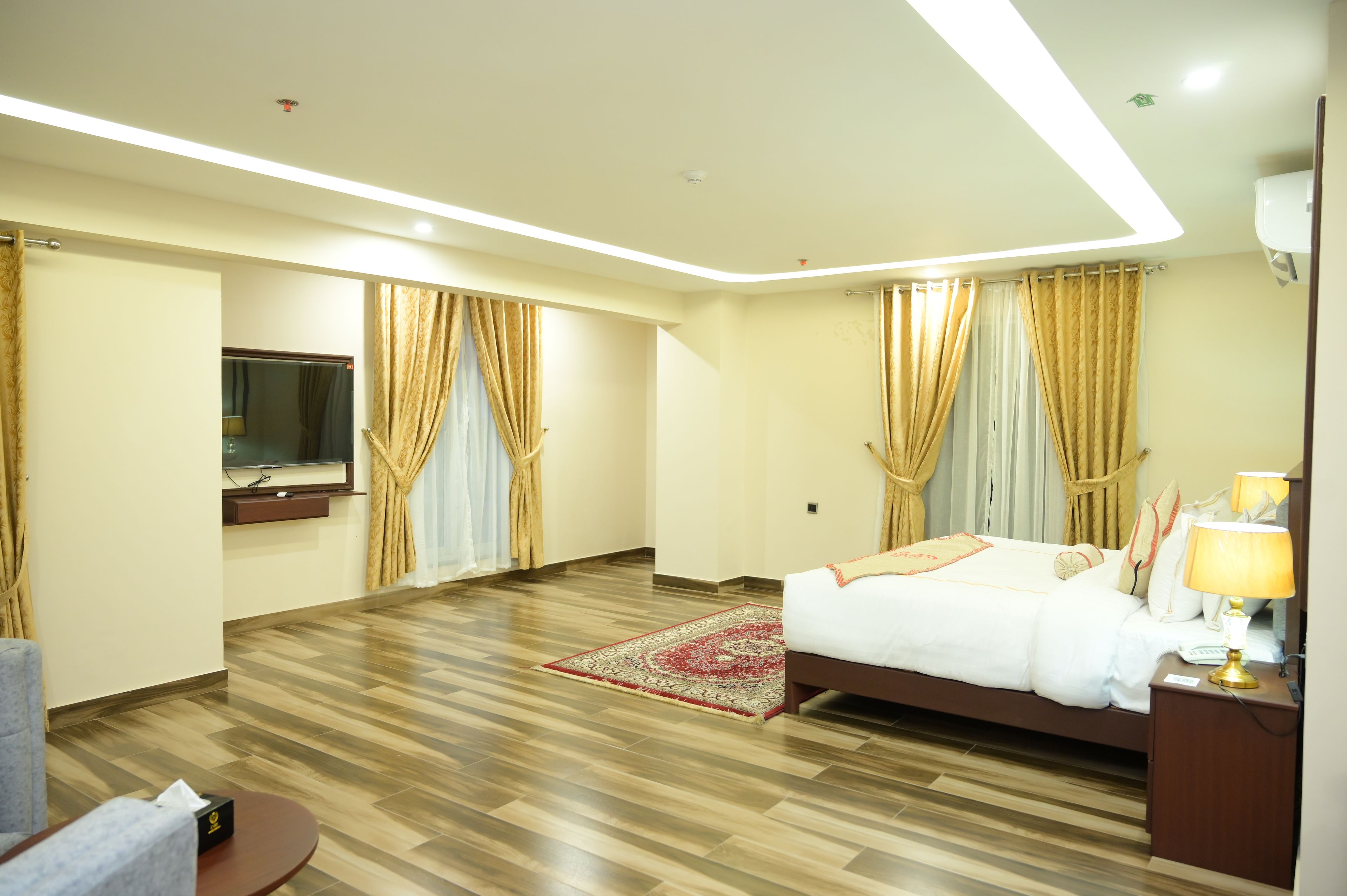 Quarto de hotel com cama, mesa de cabeceira, abajur e televisão.