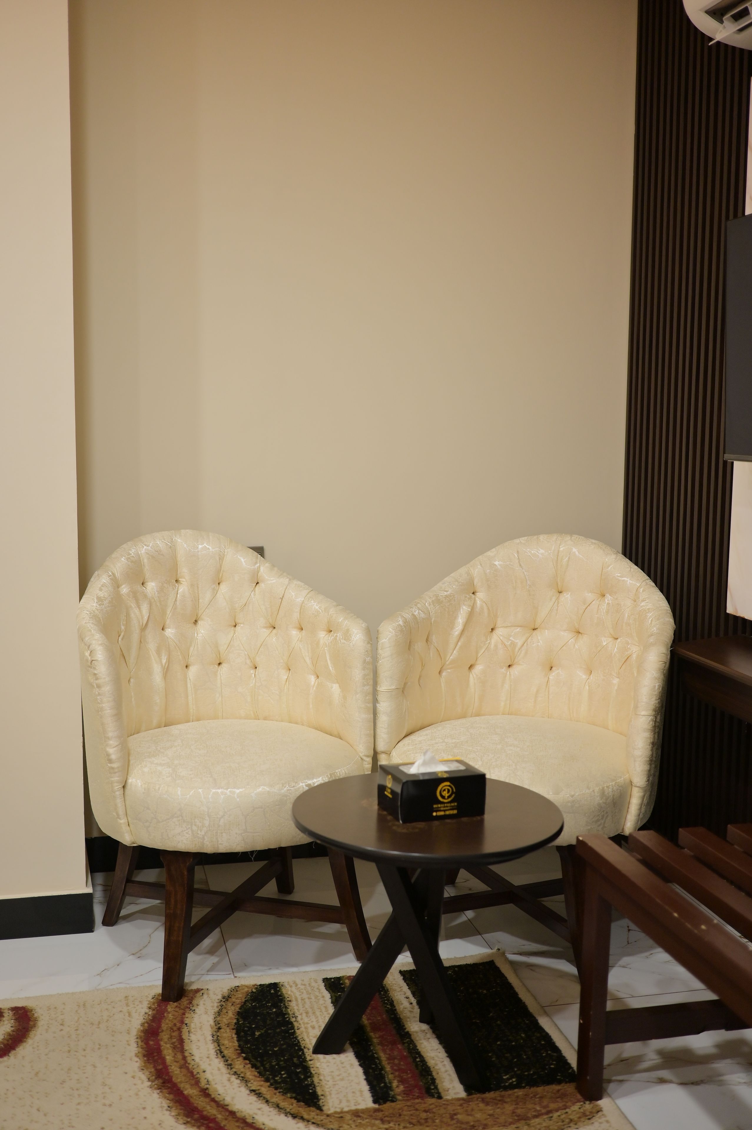 Quarto com duas poltronas estofadas viradas uma para a outra, uma mesa redonda pequena e um tapete estampado no chão.