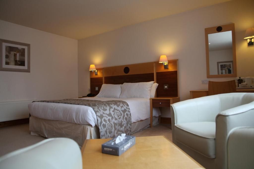 Quarto de hotel com uma cama, mesas de cabeceira, uma cadeira, uma mesinha com um estojo de lenços de papel e um espelho na parede.