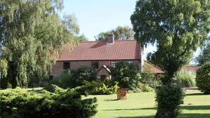 Uma casa de tijolos com telhado de telhas vermelhas, rodeada por um gramado bem cuidado e diversas árvores.