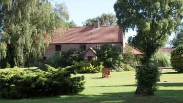Uma casa de tijolos com telhado de telhas vermelhas, rodeada por um gramado bem cuidado e diversas árvores.
