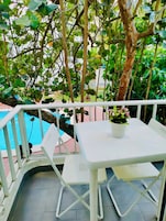 Área externa com mesas e cadeiras, um vaso de planta e vista para uma piscina.