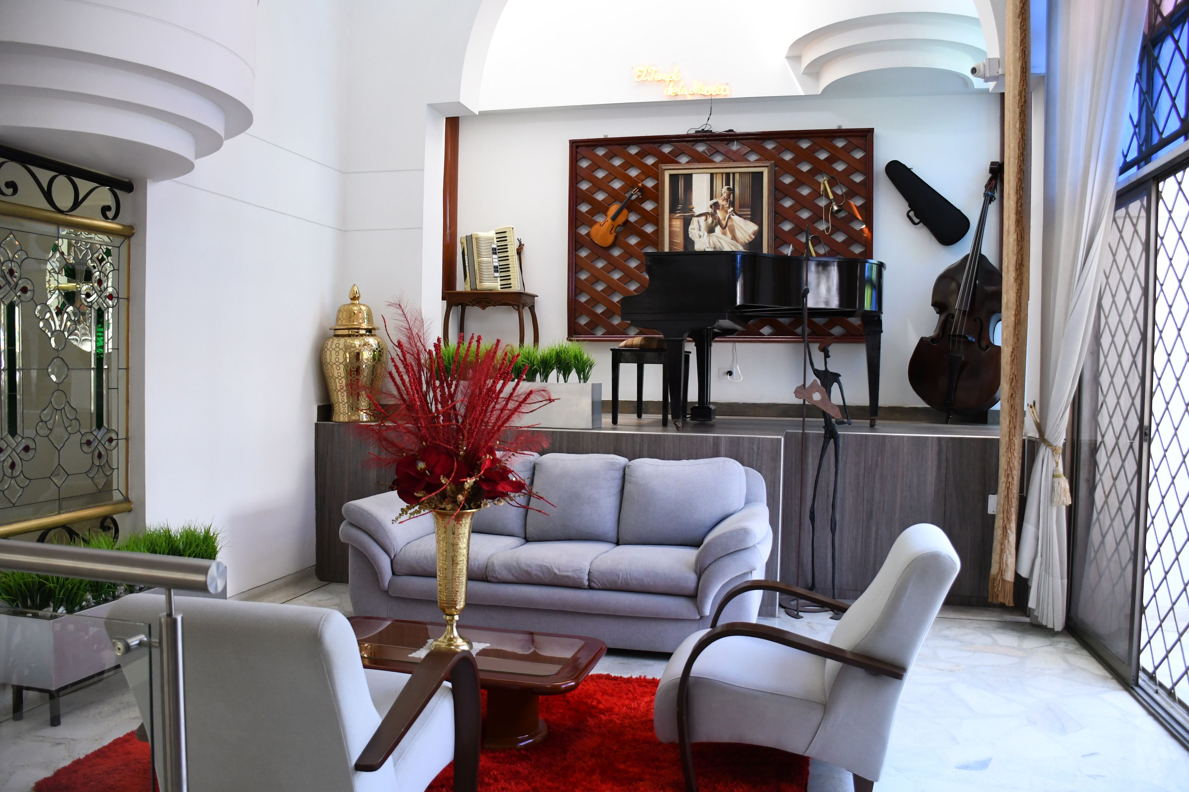 Sala de estar com sofá cinza, tapete vermelho e um piano ao fundo.