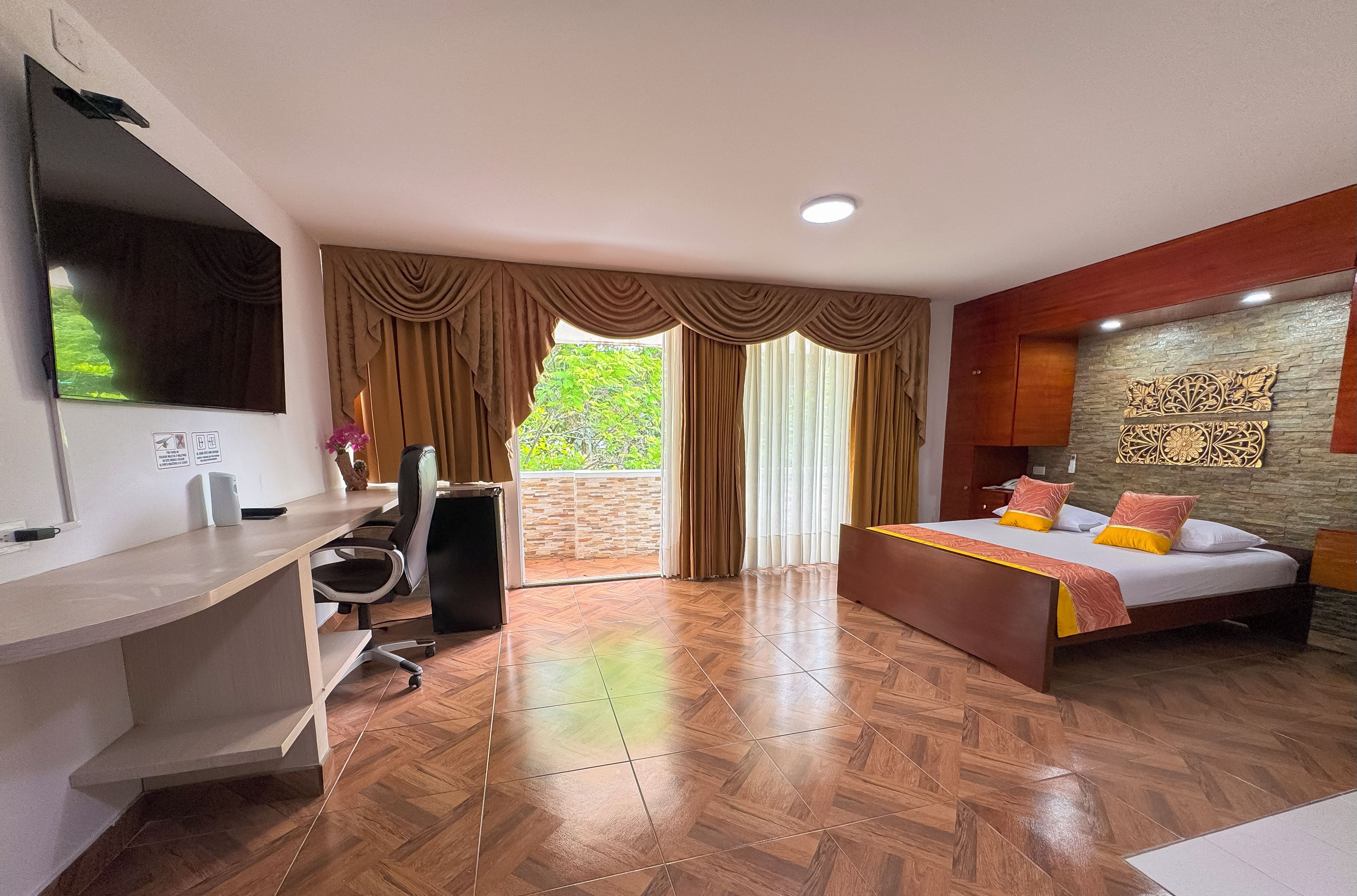 Quarto de hotel com cama, escrivaninha, cadeira e televisão.