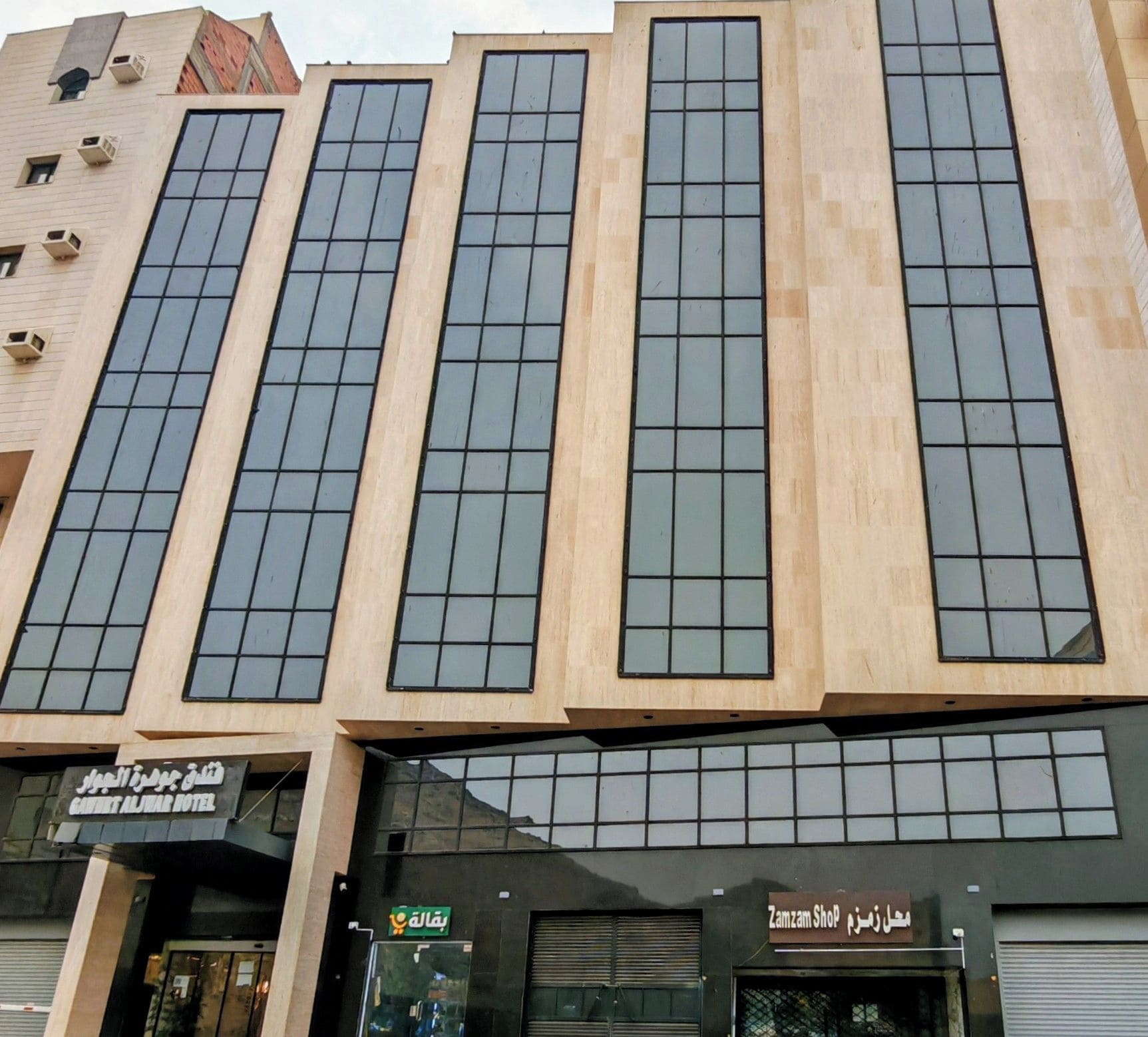Um edifício moderno com grandes janelas e a placa do Hotel Gahret Alwar.