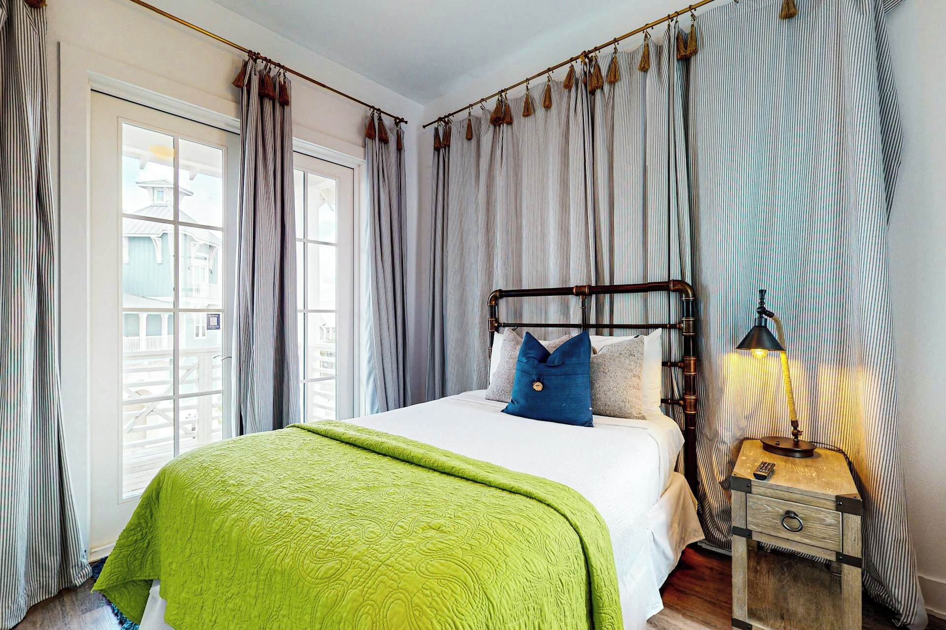 Quarto com cama, mesa de cabeceira, abajur e cortinas.