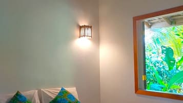 Quarto com cama, almofadas, ar condicionado, luminária na parede e janela vista para vegetação.