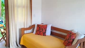 Uma cama de solteiro com colcha amarela, duas almofadas estampadas com flores e um tapete listrado e colorido.