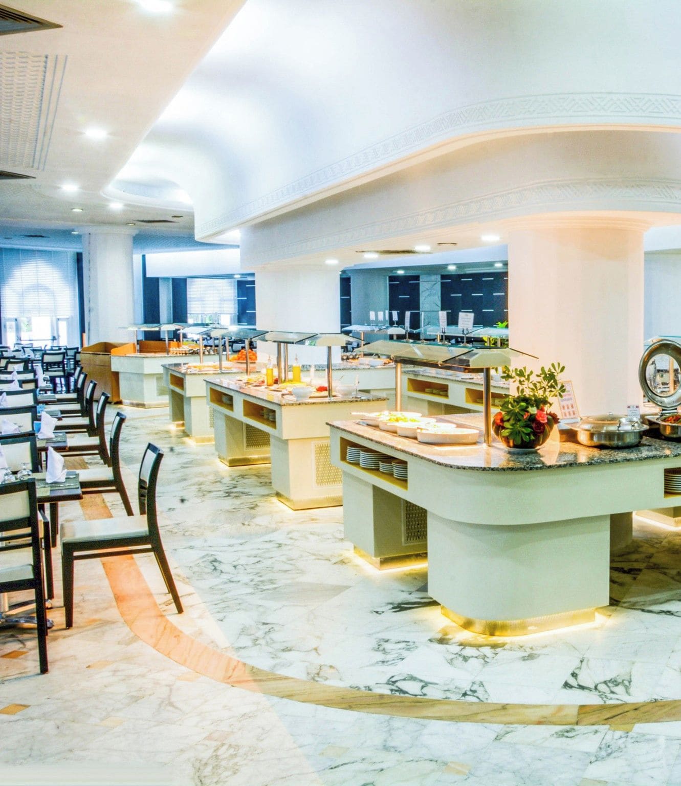 Ampla área de buffet com diversas estações de serviço e piso de mármore.