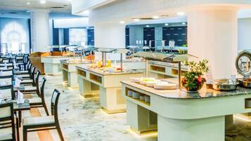 Ampla área de buffet com diversas estações de serviço e piso de mármore.