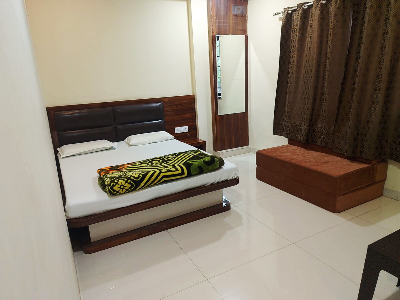 Quarto de hotel com cama, um banquinho, espelho e cortinas.