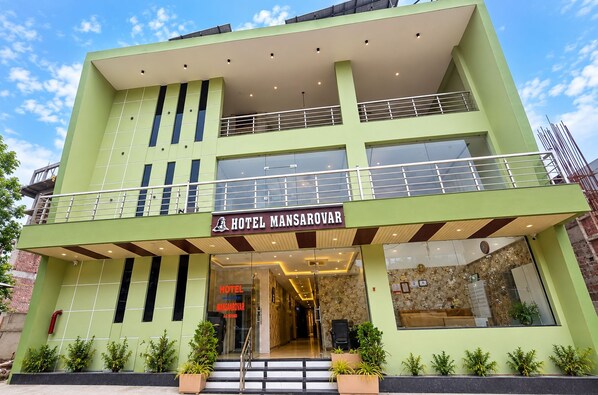 Um hotel de dois andares com fachada verde, entrada visível e uma placa com a inscrição 'HOTEL MANSAROVAR'.