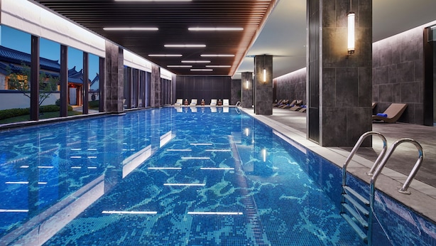 Piscina interna com água cristalina, rodeada por espreguiçadeiras e design arquitetônico moderno.