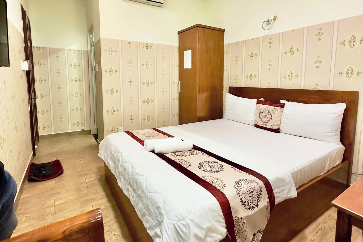 Quarto de hotel com cama, guarda-roupa de madeira, escrivaninha e cadeira.