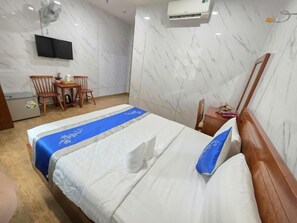 Quarto de hotel com cama, escrivaninha, cadeira, televisão e ar condicionado.