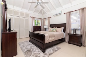 Quarto com cama, penteadeira, mesa de cabeceira, ventoinha no teto e janela com cortinas.
