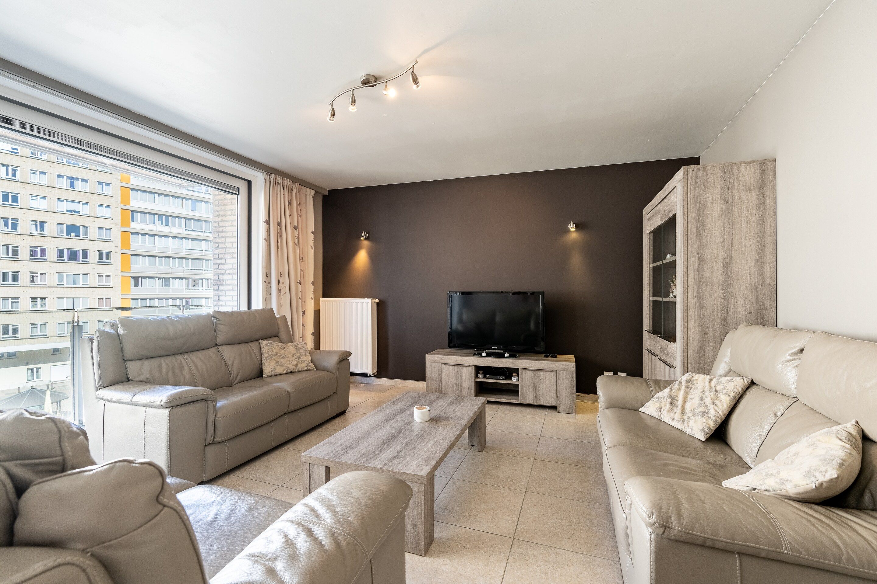 Uma sala de estar moderna com sofá, mesa de centro, televisão e armário.