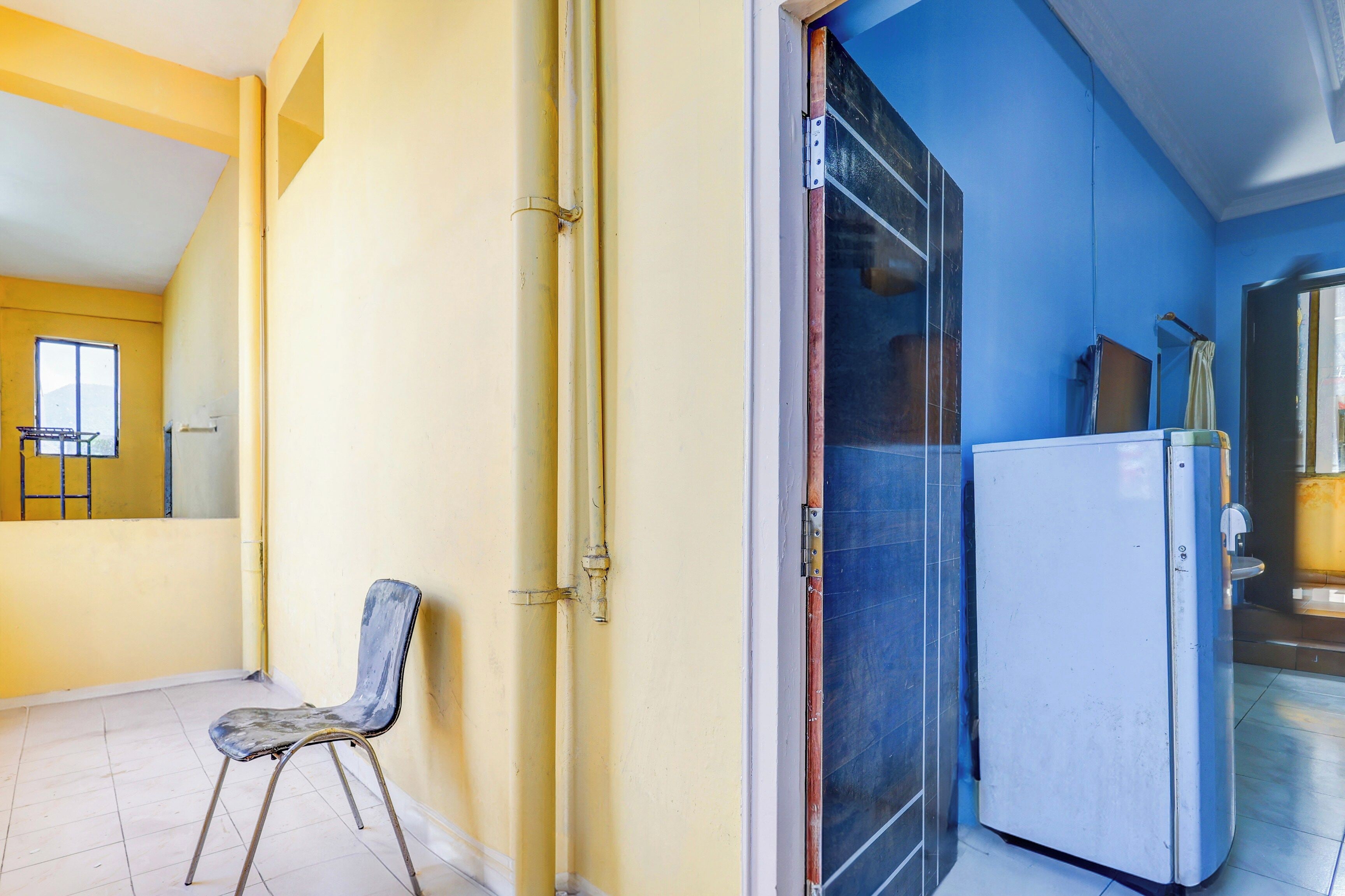Quarto com uma cadeira, um refrigerador e uma porta que dá para outro cômodo.