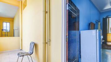 Quarto com uma cadeira, um refrigerador e uma porta que dá para outro cômodo.