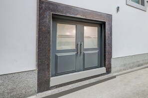Porta dupla com painel de vidro fosco, emoldurada em base de concreto, contra uma parede branca com borda de pedra texturizada.