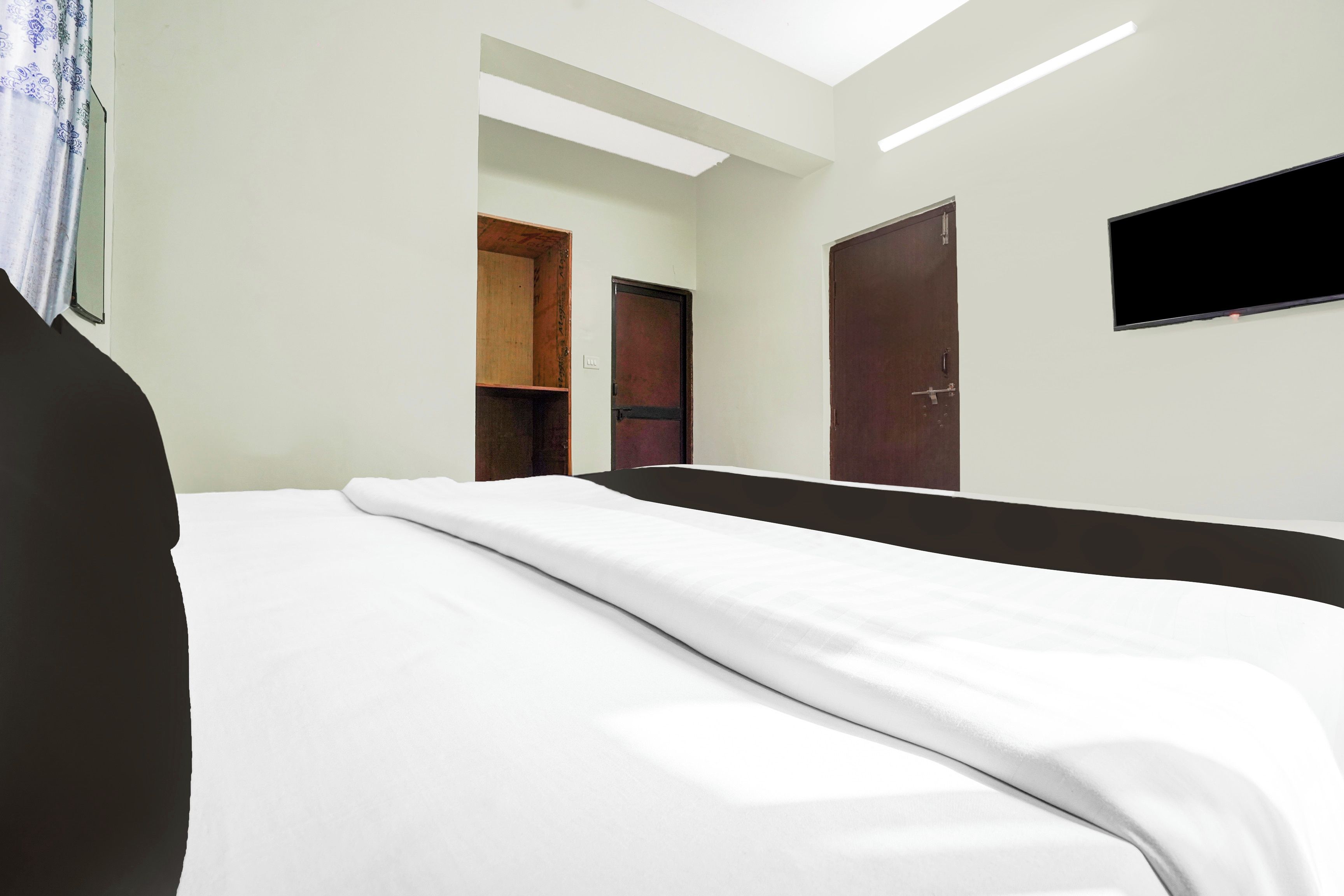 Quarto de hotel com cama, guarda-roupa, televisão na parede e janela com cortinas.