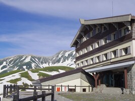 Um hotel com vista para montanhas, apresentando um estilo arquitetônico tradicional com entrada imponente e fachada de pedra.