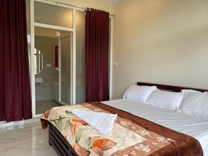 Quarto de hotel com uma cama, banheiro com porta de vidro e cortinas vermelhas.