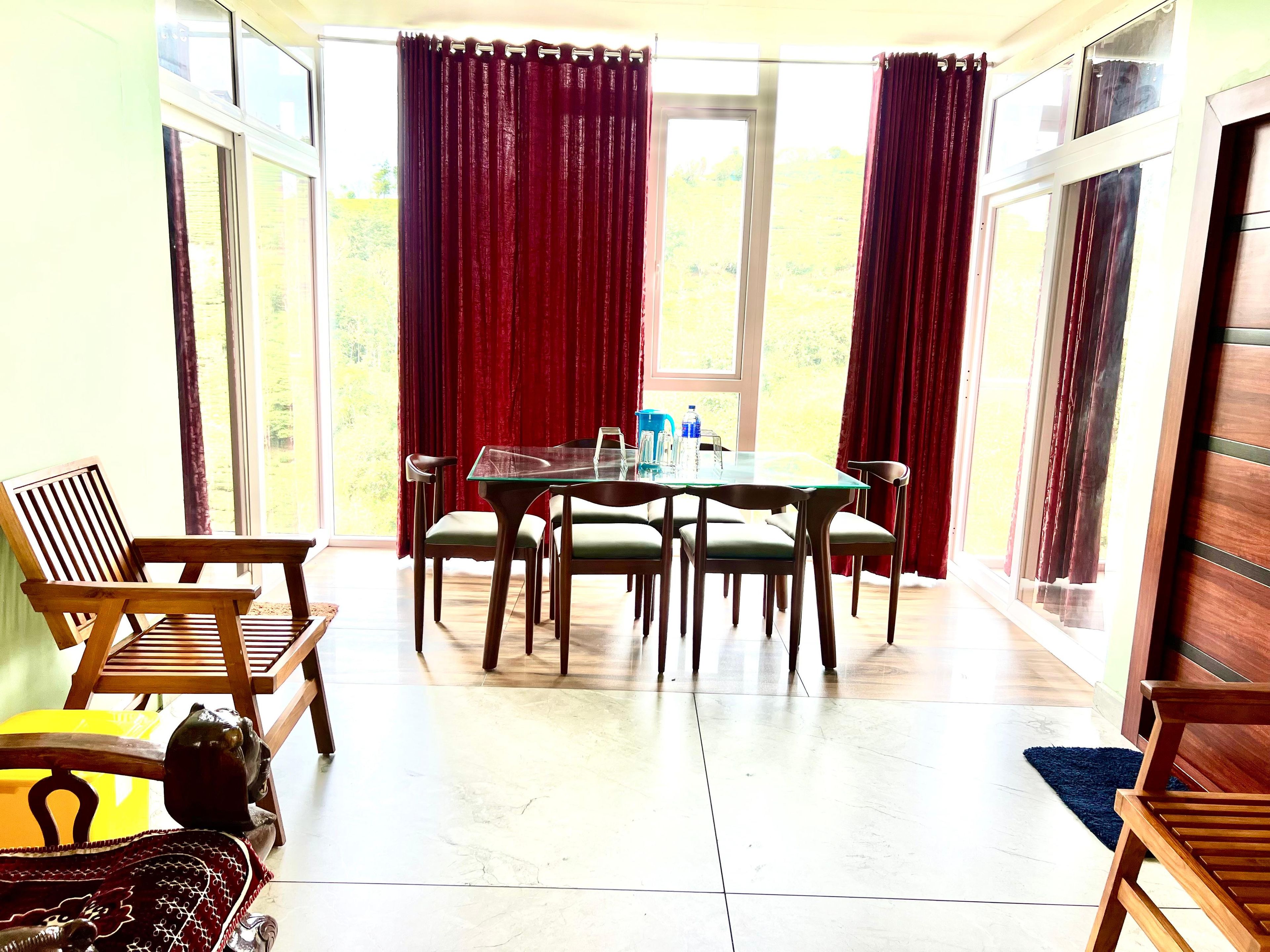 Uma sala de jantar com mesa de vidro, seis cadeiras e cortinas vermelhas.