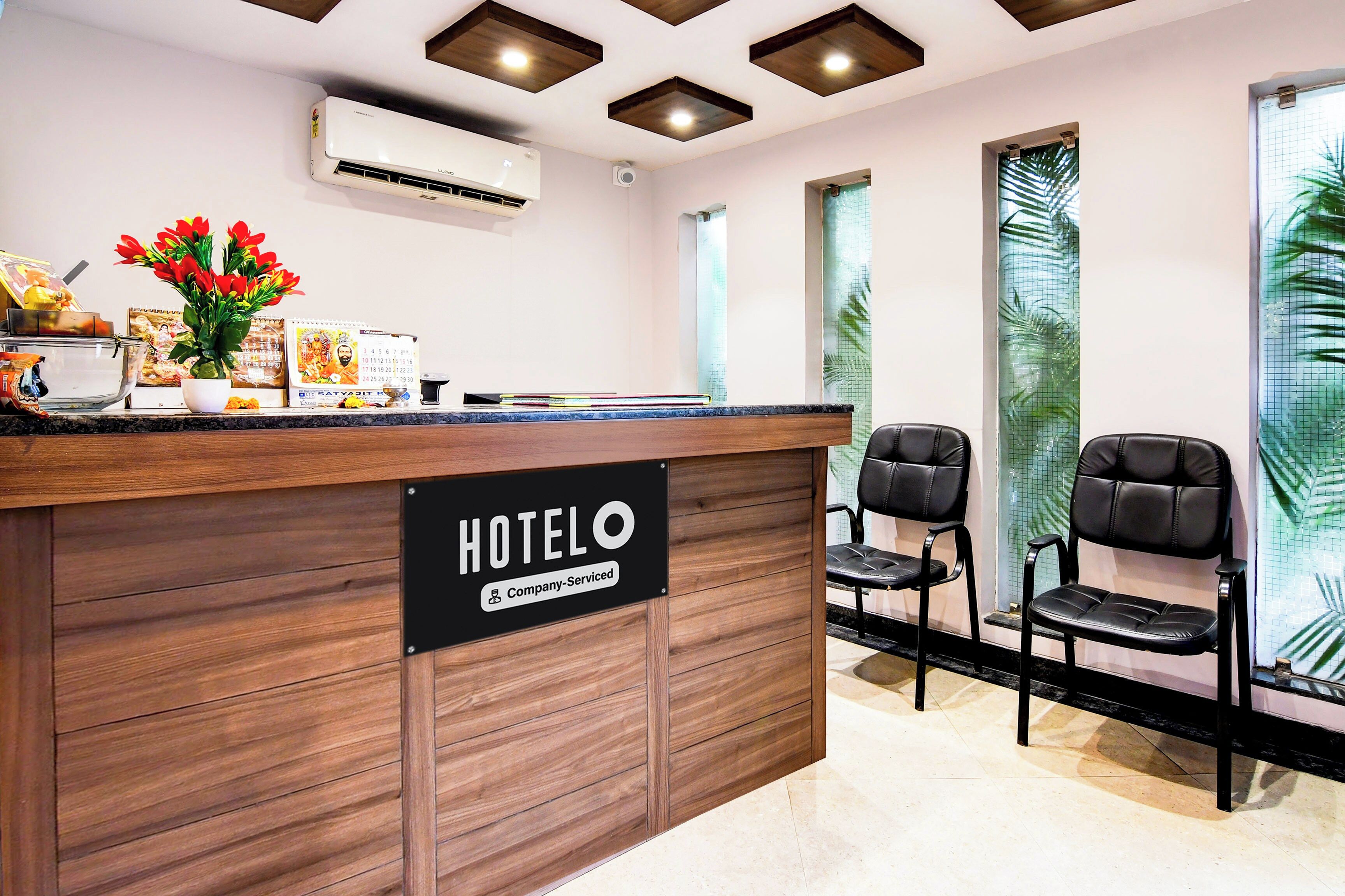 Bancada de recepção de hotel com acabamento em madeira, placa indicando serviço corporativo e duas cadeiras pretas à direita.