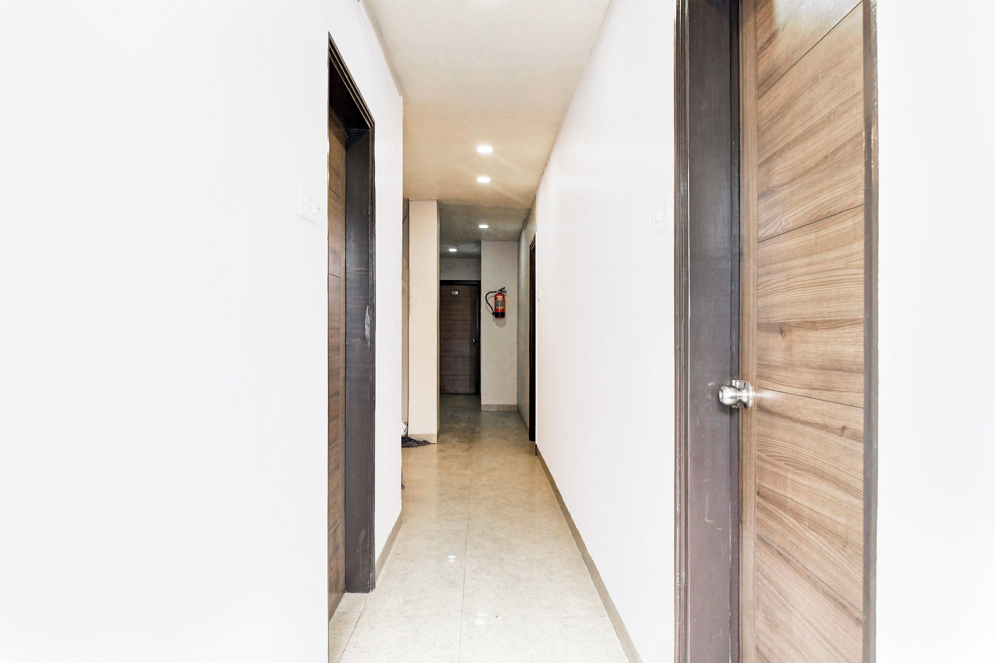 Um corredor com uma porta de madeira à direita e um extintor de incêndio fixado na parede.
