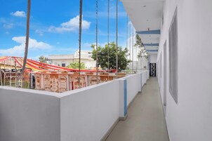 Corredor com vista para um edifício com telhado vermelho e andaimes, uma parede branca com faixa azul e uma porta com design preto e branco.