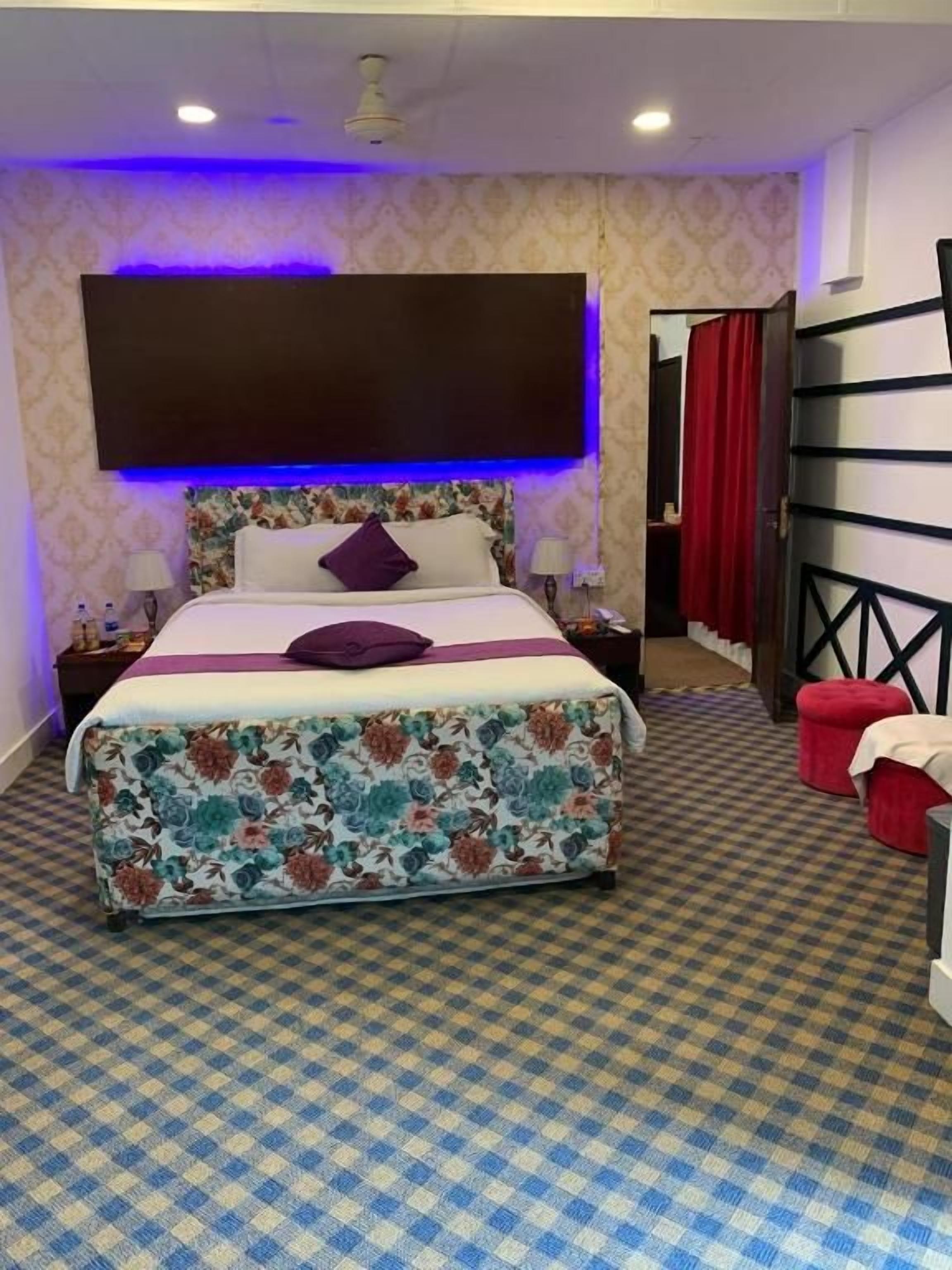 Quarto com cama, televisão de tela plana na parede, carpete estampado e cortina vermelha.