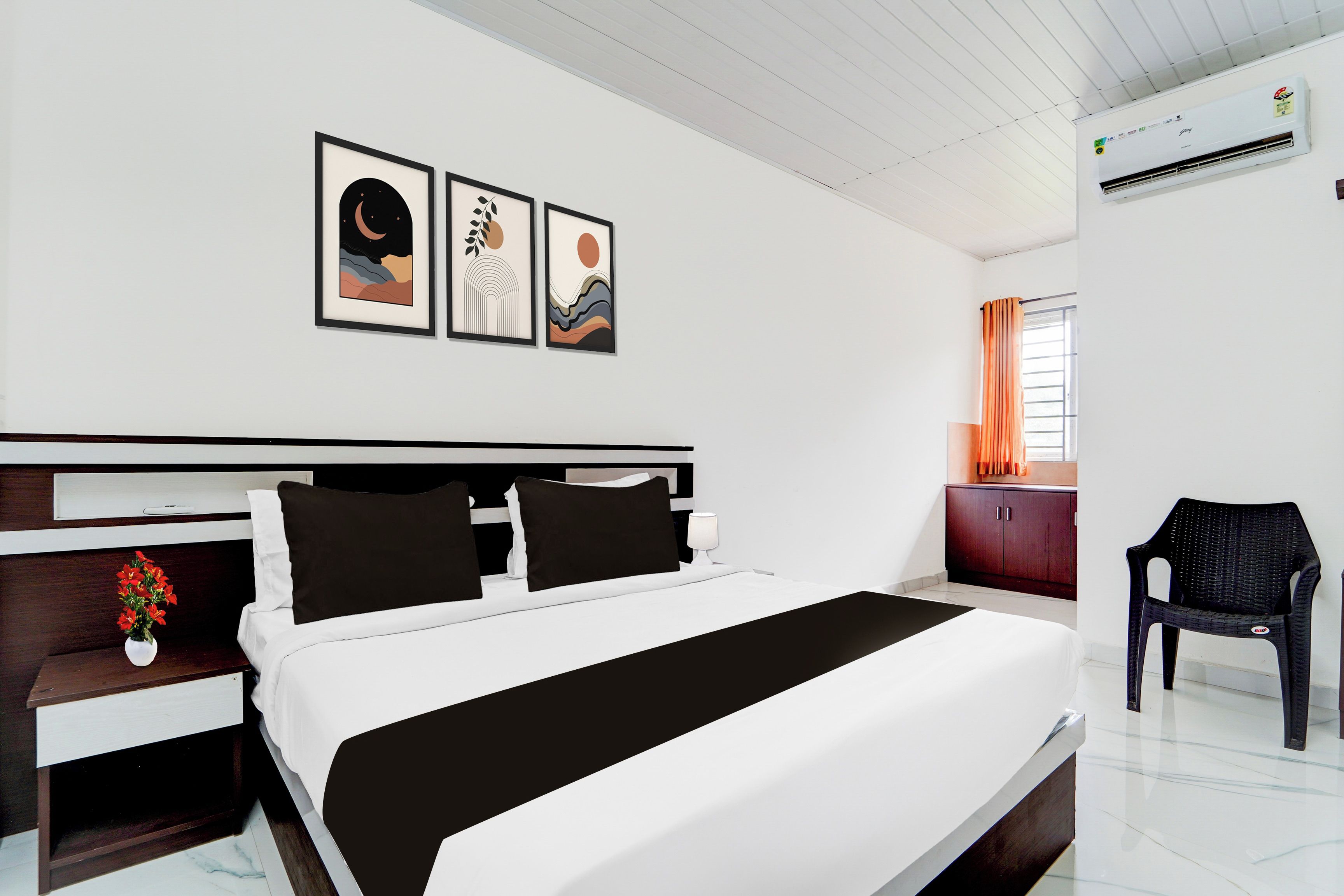 Quarto de hotel moderno com uma cama grande, mesa de cabeceira com um vaso de flores, guarda-roupa e uma cadeira.