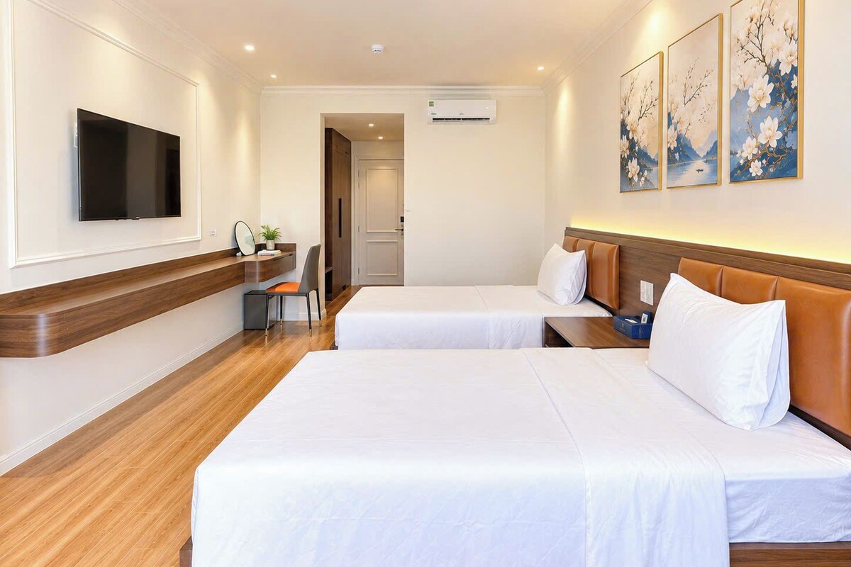 Quarto de hotel com duas camas, televisão de tela plana, escrivaninha com cadeira e obras de arte na parede.
