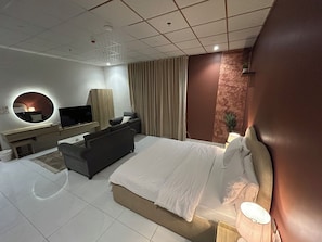 Quarto de hotel moderno com uma cama grande, televisão, escrivaninha e espelho redondo na parede.