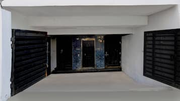 Um corredor estreito com persianas de metal preto fechadas em ambos os lados, dando para uma porta escura.