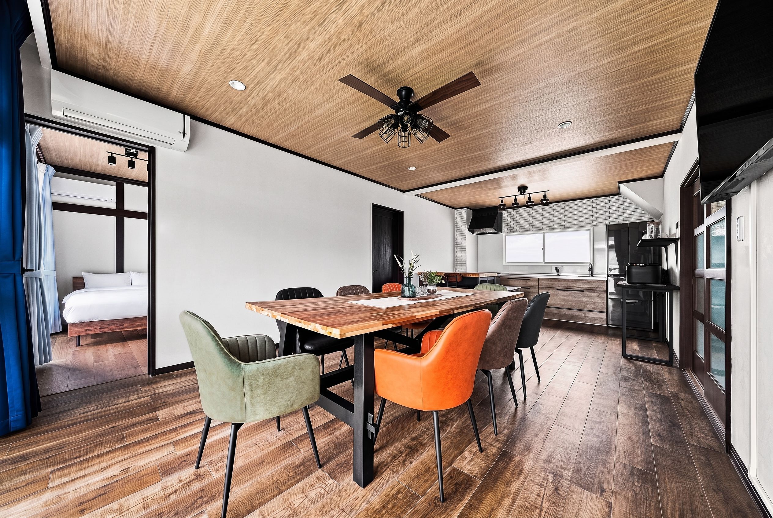 Cozinha moderna com teto de madeira, área de refeições com mesa de madeira e cadeiras coloridas, e bancada de cozinha visível.