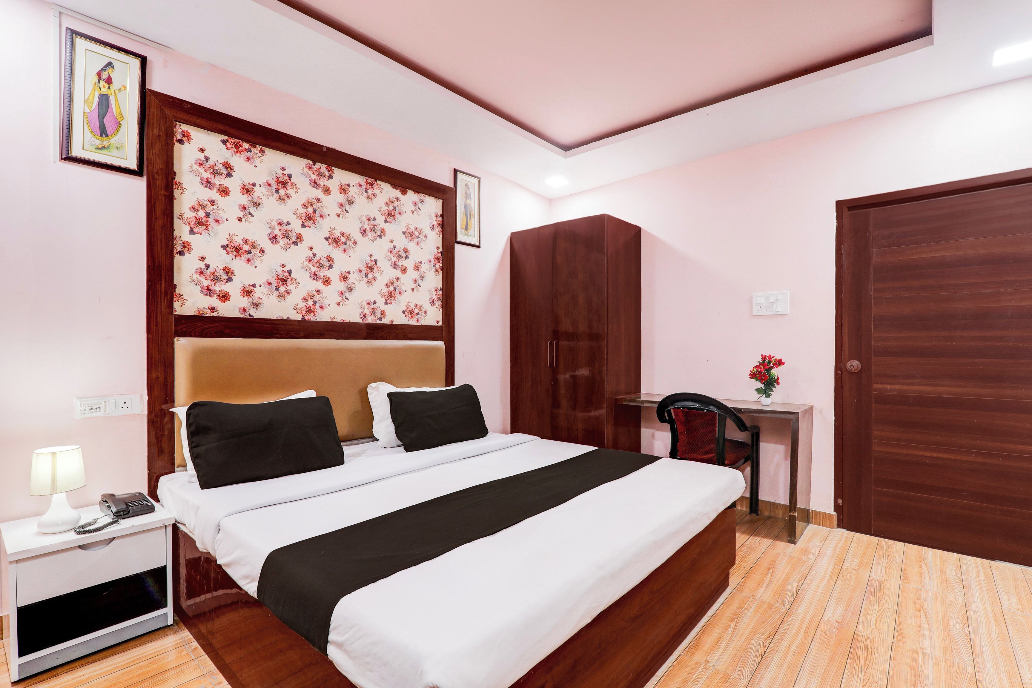 Quarto de hotel com cama, mesa de cabeceira, luminária, telefone e escrivaninha com cadeira.
