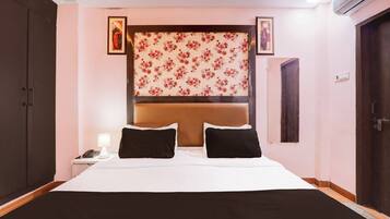 Quarto de hotel com cama, mesa de cabeceira, abajur e duas fotos emolduradas na parede.