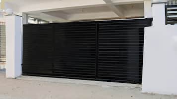 Um portão preto fechado, com uma parede branca e chão de concreto.