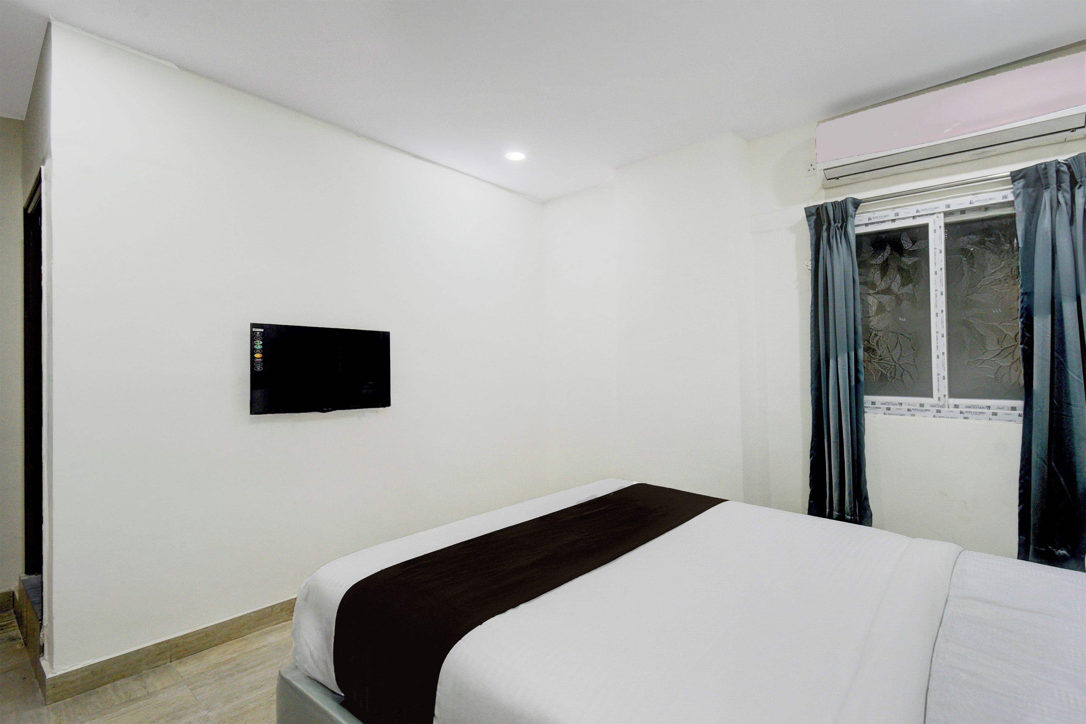 Quarto de hotel com cama, televisão de tela plana na parede e janela com cortinas.