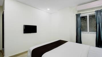 Quarto de hotel com cama, televisão de tela plana na parede e janela com cortinas.