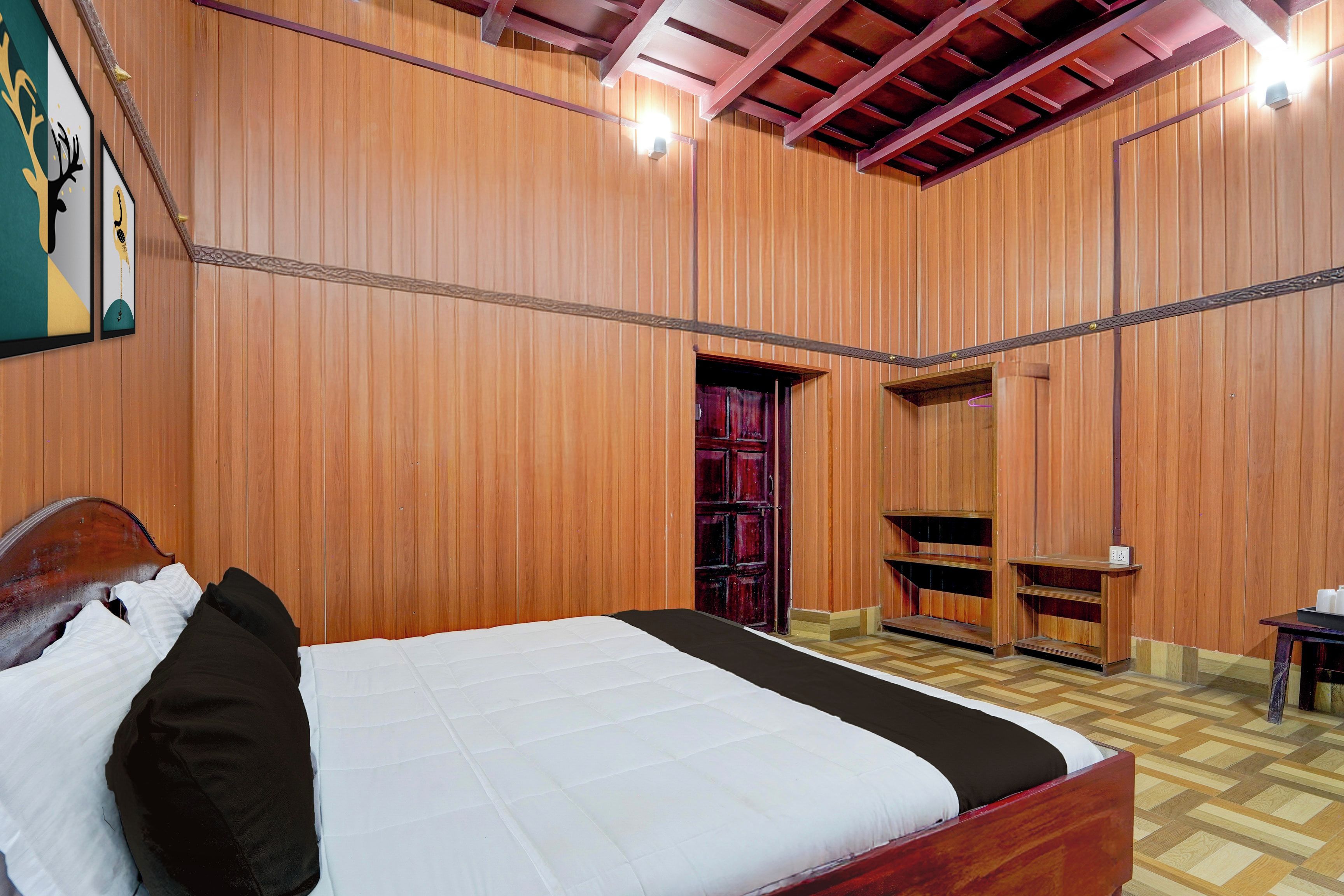 Quarto com paredes de madeira, cama com roupa de cama preta e branca, cabeceira de madeira, cômoda de madeira e espelho na parede.