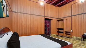 Quarto com paredes de madeira, cama com roupa de cama preta e branca, cabeceira de madeira, cômoda de madeira e espelho na parede.